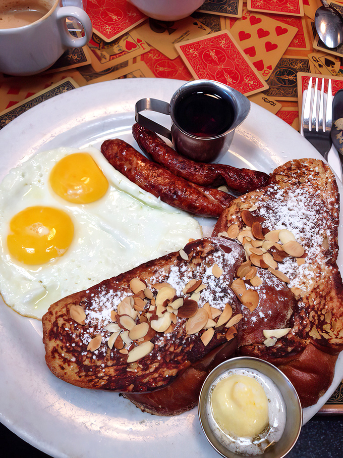 Breakfast harmony achieved: sunny-side-up eggs, savory sausage links, and French toast dusted with powdered sugar and sliced almonds.