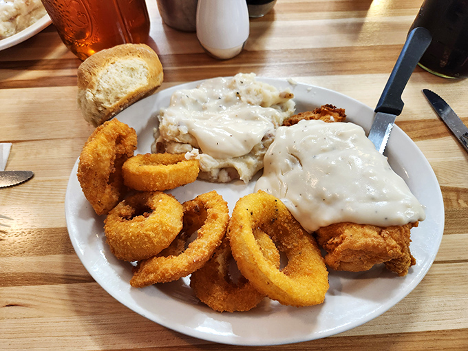 Country-fried steak smothered in gravy with golden onion rings—a plate that says "diet starts tomorrow" in the most delicious way possible.