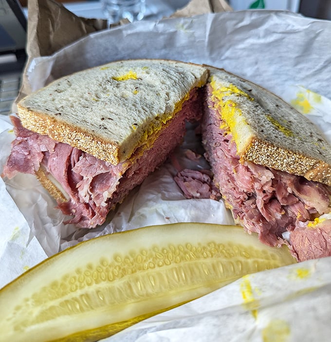 The star of the show in all its glory—layers of perfectly pink corned beef stacked between rye bread with a pickle standing guard. Architecture you can eat.