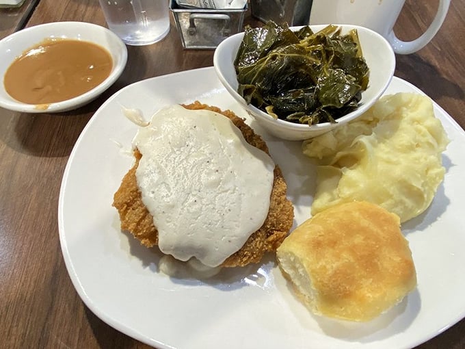 Southern comfort on a plate: country fried steak smothered in creamy gravy, alongside collard greens and mashed potatoes. The biscuit isn't optional—it's essential.