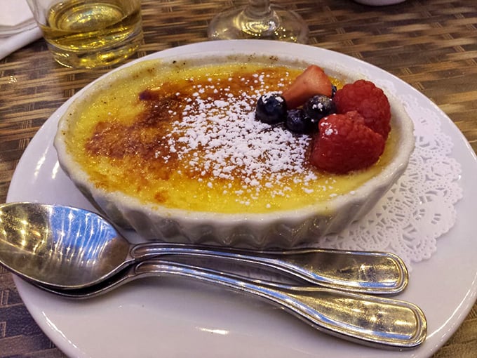 Crème brûlée with that perfect glass-like sugar crust waiting to be shattered. The berries aren't just garnish—they're little flavor bombs cutting through the richness.