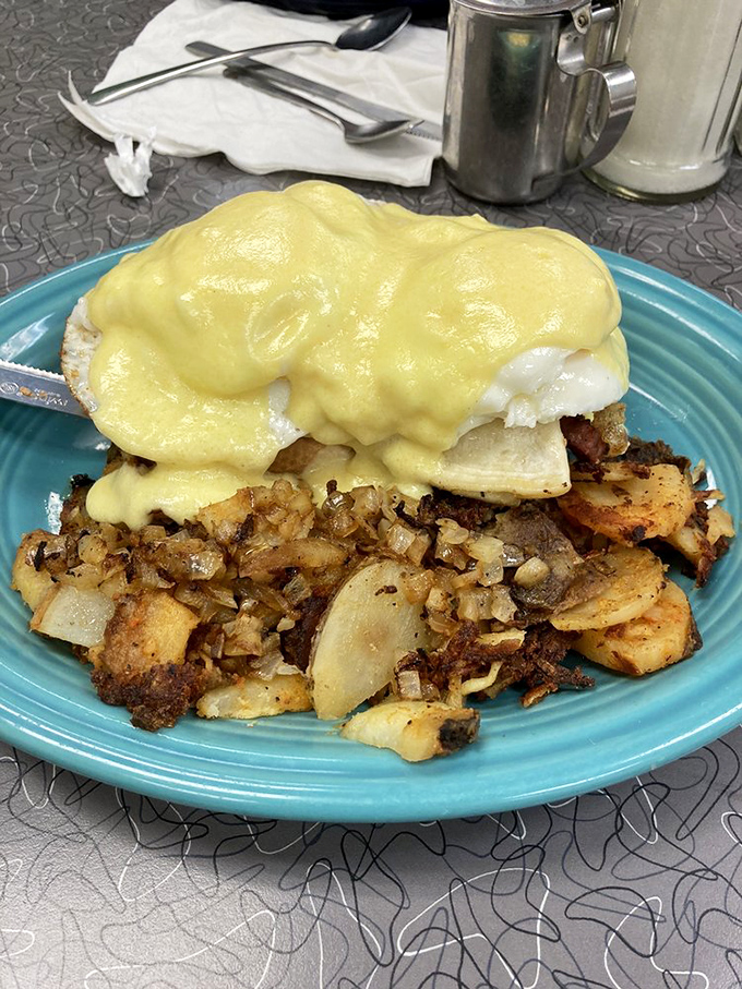 Behold the holy grail of breakfast – Eggs Benedict with hollandaise cascading like a golden waterfall over perfectly poached eggs and crispy home fries.
