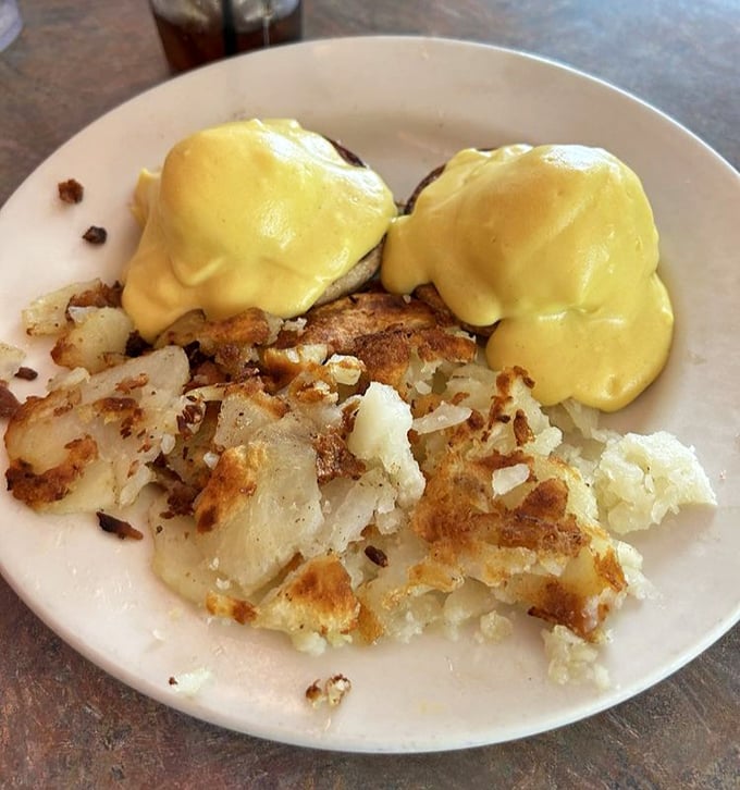 Eggs Benedict done diner-style—a golden hollandaise waterfall cascading over English muffins, with home fries crisped to that perfect sweet spot between tender and crunchy.
