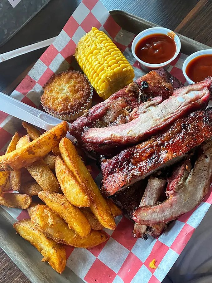 Behold the holy trinity of barbecue bliss: perfectly smoked ribs with that telltale pink smoke ring, crispy fries, and corn on the cob to round out the experience.
