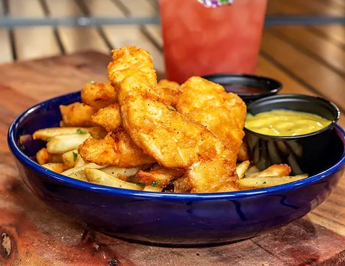 Golden-battered haddock perched atop a mountain of fries – this isn't just fish and chips, it's edible sunshine that crunches in all the right places.