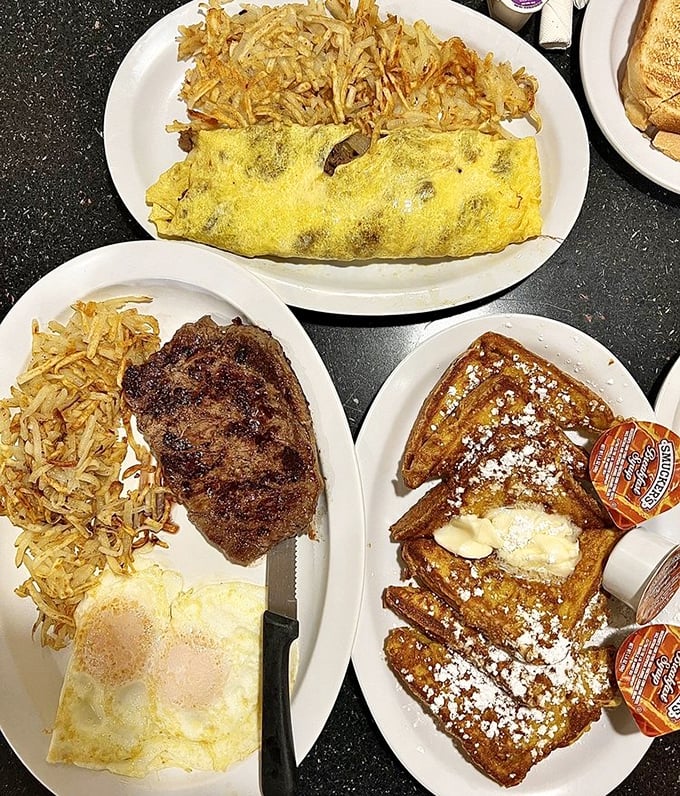 Breakfast symphony in three movements: a fluffy omelet, perfectly seared steak, and French toast dusted with powdered sugar—the holy trinity of morning indulgence.