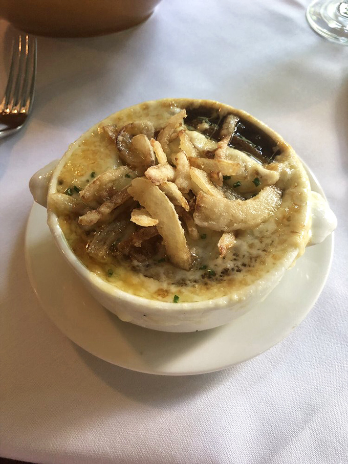 The legendary French onion soup arrives like a work of art – that golden, bubbling cheese canopy hiding a treasure trove of caramelized goodness below.