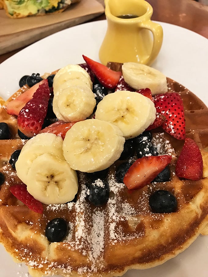 Breakfast nirvana achieved! This waffle doesn't just have fruit on top—it's practically hosting a berry-banana summit meeting under a gentle snowfall of powdered sugar.