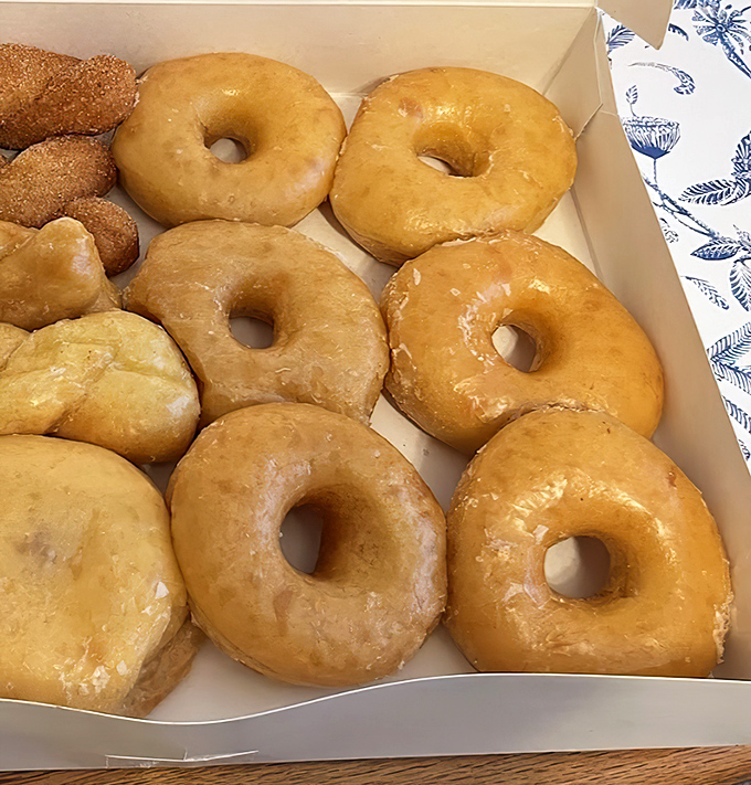 Golden-hued glazed donuts nestled in their box like edible sunshine—each one a perfect circle of joy waiting to transform your ordinary morning.