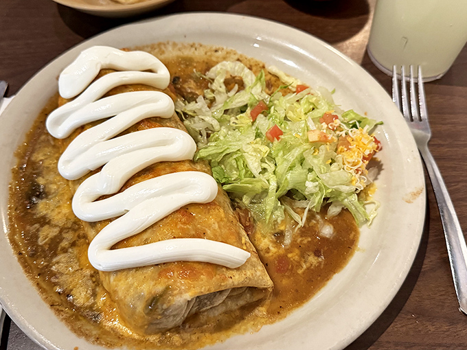 Behold the green chili burrito masterpiece - golden tortilla embracing tender filling, crowned with cooling sour cream swirls of perfection.