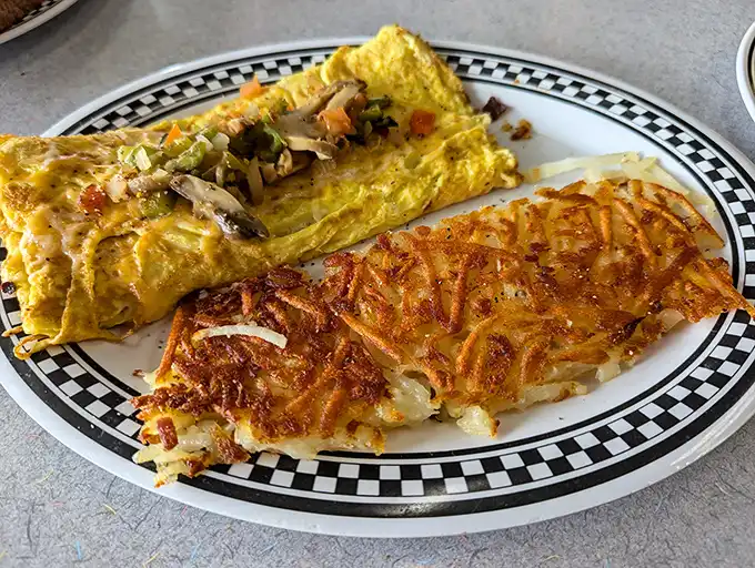 The holy grail of breakfast: perfectly crispy hash browns alongside a veggie-packed omelet. This plate represents everything right with American diner culture.