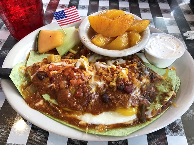 Behold the star attraction: a spinach tortilla cradling eggs beneath a blanket of chili, cheese, and salsa—breakfast nirvana with a tiny American flag salute.
