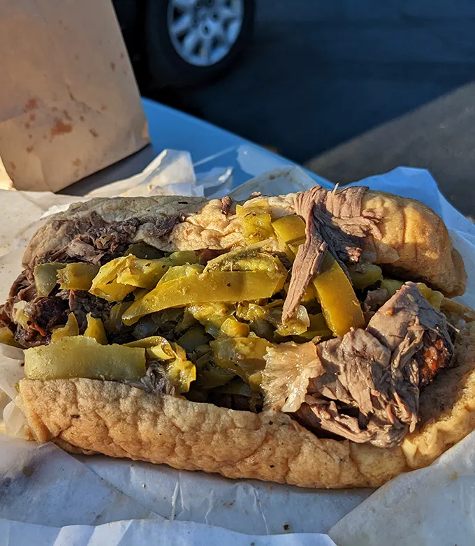 Behold the holy grail—thin-sliced beef swimming in savory jus, crowned with vibrant peppers, all nestled in bread that somehow maintains structural integrity.