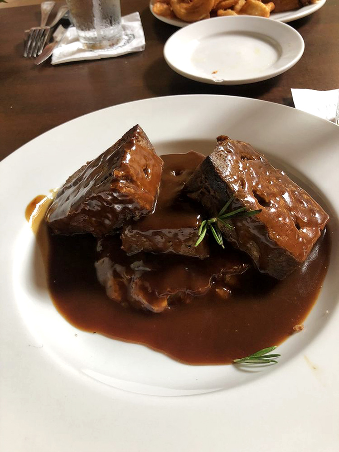 The legendary meatloaf arrives like a celebrity – glistening with gravy, perfectly sliced, and garnished with a sprig of rosemary for that touch of class.
