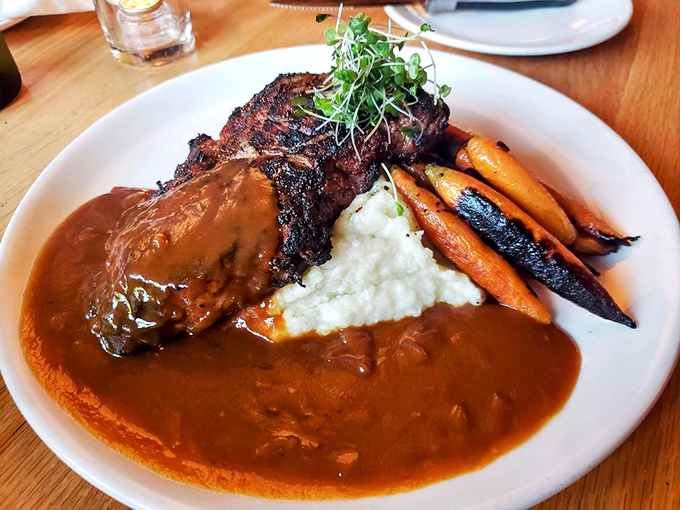 This isn't just a steak, it's a masterpiece of fire and beef—wood-grilled NY strip nestled on whipped potatoes with charred carrots and a pool of savory onion gravy.