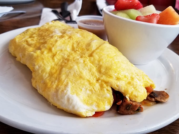 This isn't just an omelet—it's a fluffy golden envelope delivering a secret message of deliciousness. The fresh fruit side is just showing off.