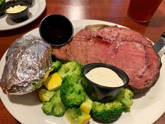 Behold the star of the show: perfectly pink prime rib accompanied by fresh broccoli, a baked potato in foil, and that essential horseradish sauce that clears sinuses and elevates beef.