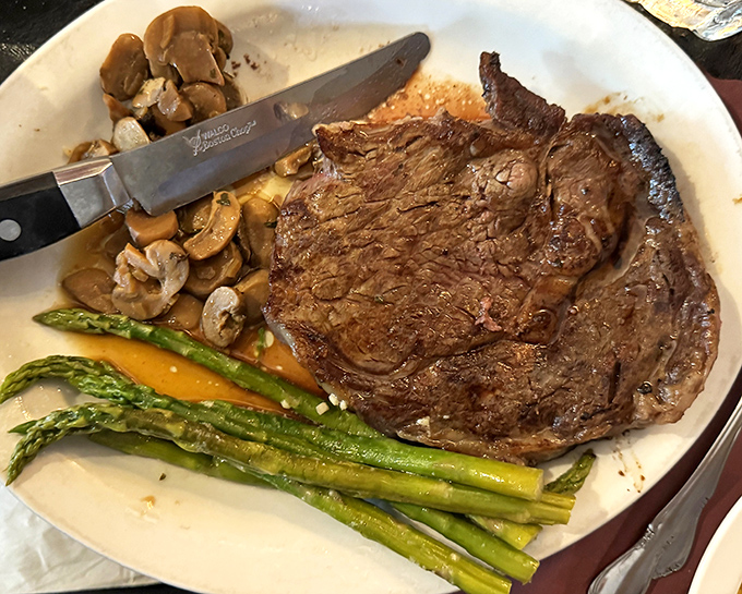 A perfectly seared ribeye shares the plate with sautéed mushrooms and asparagus – the holy trinity of steakhouse bliss.