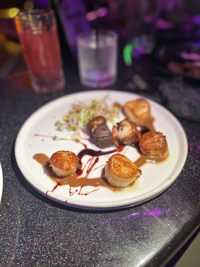 Perfectly seared scallops dance with savory pork medallions on a plate artfully streaked with sauces. Culinary drama at its finest!