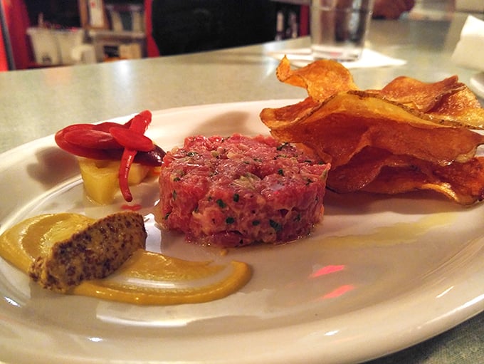 The steak tartare arrives like edible jewelry—ruby-red perfection with mustard and house-made chips that shatter satisfyingly between your teeth.