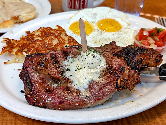 Behold the star attraction: a perfectly seared steak with melting herb butter, sunny-side eggs, and hash browns that achieve the golden-crisp ideal.