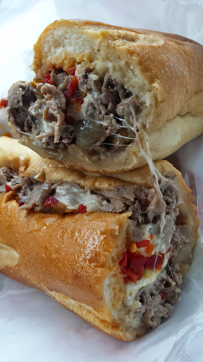 The cheesesteak in its natural habitat—tender ribeye embraced by melted cheese and nestled in a perfect roll. This is the sandwich Philadelphia built its reputation on.