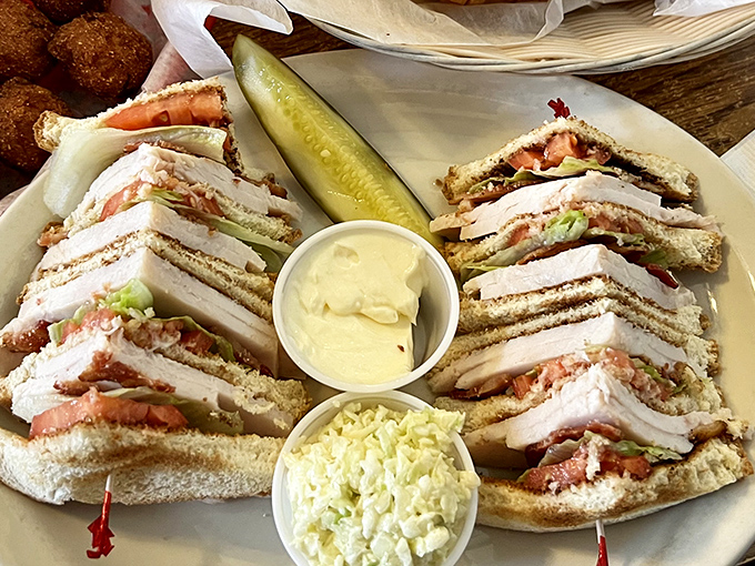 The legendary club sandwich arrives like architecture on a plate – perfectly stacked layers of goodness with enough filling to make you wonder how to approach it.
