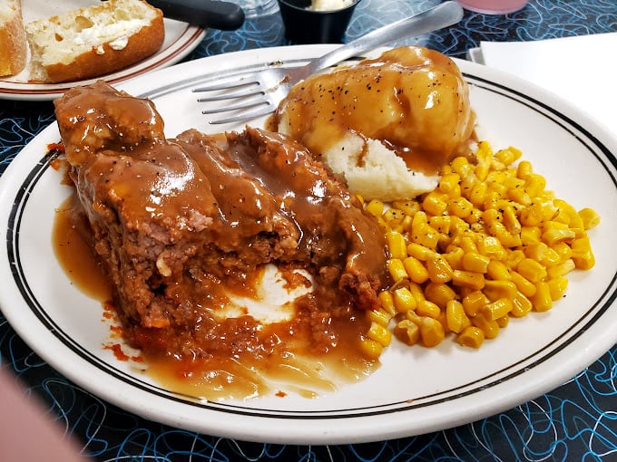 Behold the meatloaf that launched a thousand road trips! Smothered in gravy with mashed potatoes and corn—comfort food nirvana achieved.