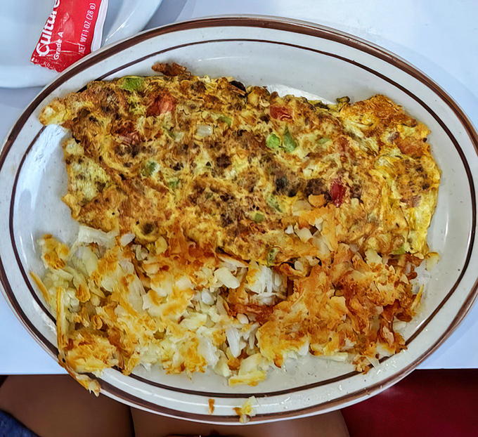 This isn't just an omelet—it's an architectural marvel of eggs, perfectly folded around a treasure trove of fillings and flanked by golden hash browns.