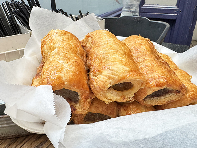 Golden, flaky sausage rolls basking in their paper-lined glory – architectural masterpieces that shatter with that first, perfect bite.
