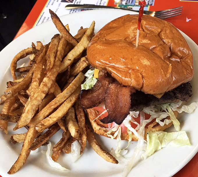 This isn't just a burger—it's architecture. Golden fries standing tall beside a bacon cheeseburger that requires both hands and a strategy.