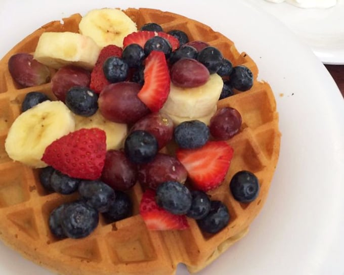This waffle arrives dressed to impress – fresh fruit crowning golden squares of breakfast perfection.