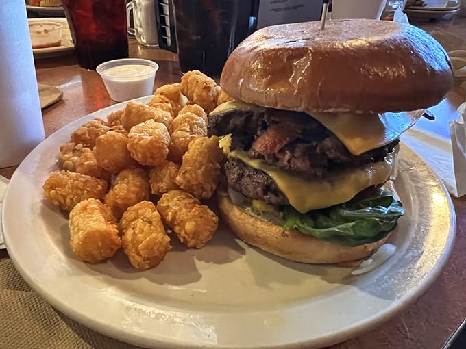 A burger that requires both hands and possibly a strategy session. That cheese melt is performing at Olympic levels while those tater tots stand by in golden support.