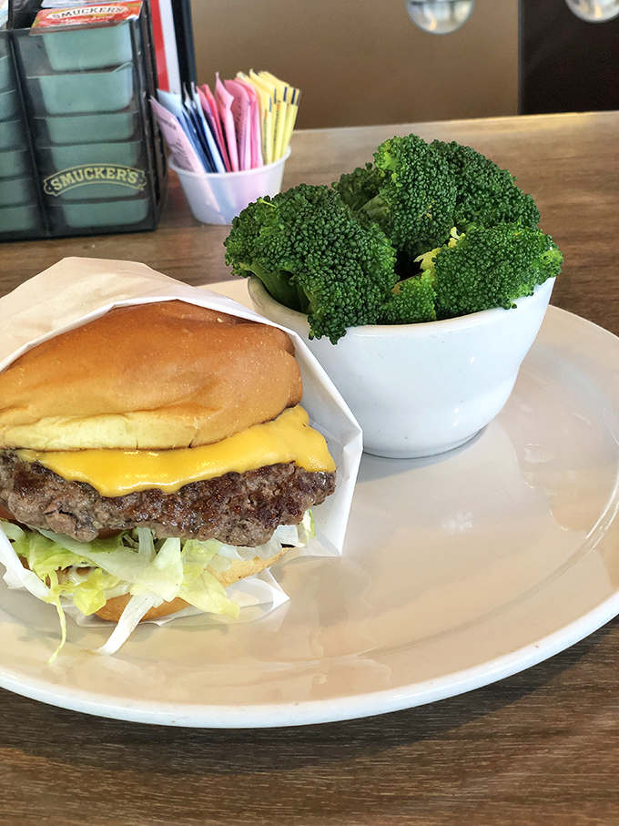 Behold the cheeseburger in its natural habitat—perfectly melted American cheese on a hand-formed patty. That broccoli is fooling nobody about your intentions.