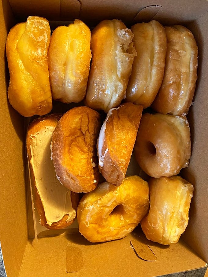 A dozen glazed donuts nestled in their cardboard cradle—like edible gold bars waiting to fund your happiness deficit.