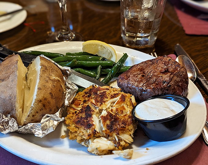 The surf meets turf in perfect harmony: a filet mignon, golden crab cake, and baked potato – the culinary equivalent of hitting the jackpot.