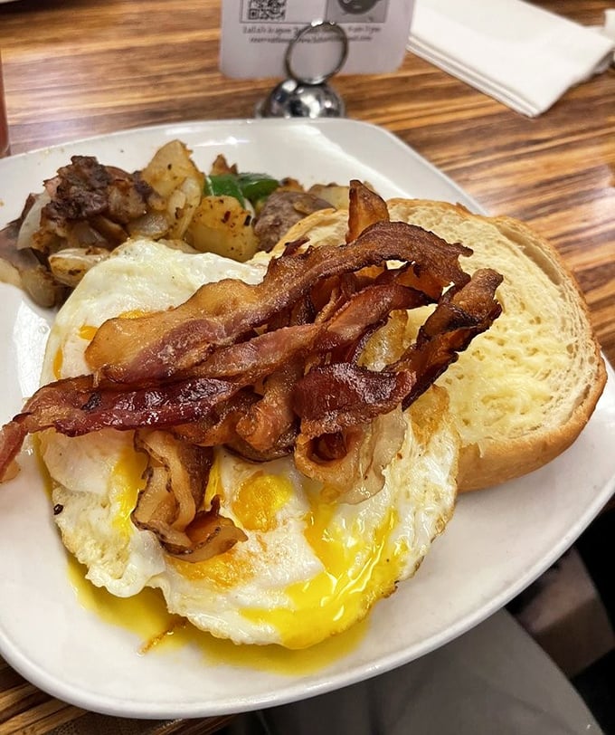 Breakfast architecture at its finest: crispy bacon, sunny eggs with yolks ready to cascade, and house potatoes that refuse to be mere sidekicks.
