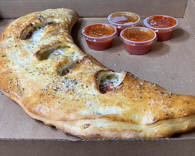 The stromboli arrives like a golden crescent moon, glistening with possibility. Four cups of marinara because one is never enough for this beauty.