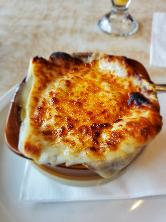 This French onion soup isn't messing around—the cheese cap is bronzed and bubbling, waiting to be broken like a crème brûlée's sugary ceiling.