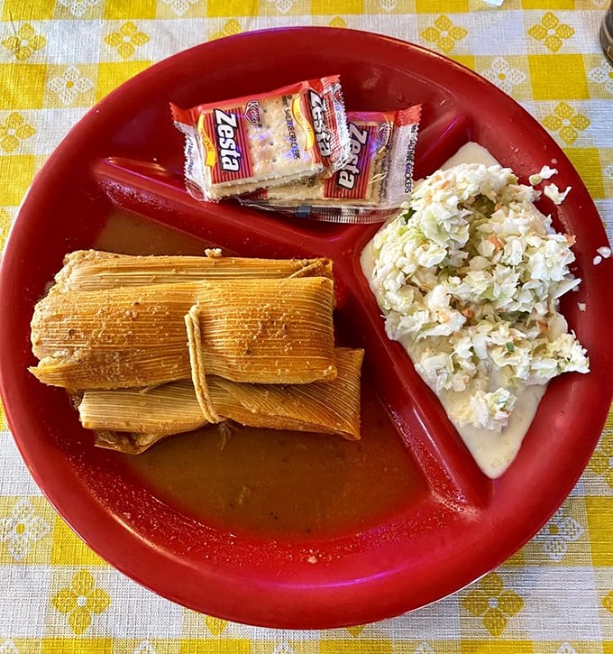 Mississippi Delta tamales nestled on a bright red plate—corn husks hiding spiced treasures alongside creamy coleslaw and crackers.