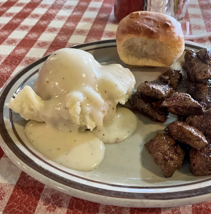 Comfort on a plate – creamy mashed potatoes swimming in gravy alongside perfectly seared steak bites, with a biscuit standing sentry.