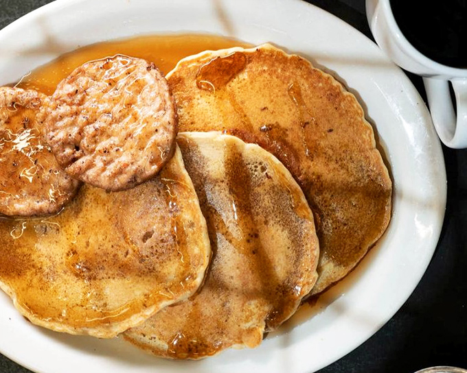 Golden pancakes with a perfectly grilled sausage patty—the kind of breakfast that makes you want to cancel your morning plans and order a second round.