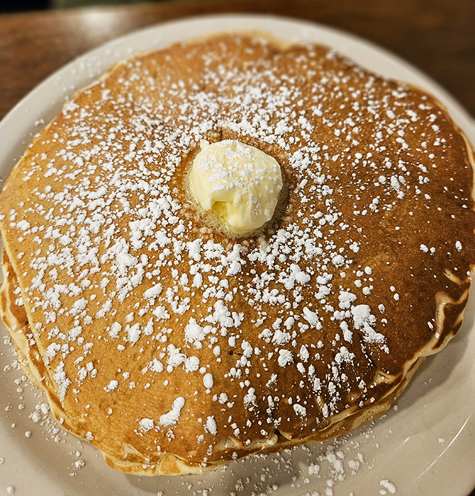 This pancake isn't just breakfast—it's a fluffy canvas of possibility, dusted with powdered sugar and crowned with a melting pat of butter.