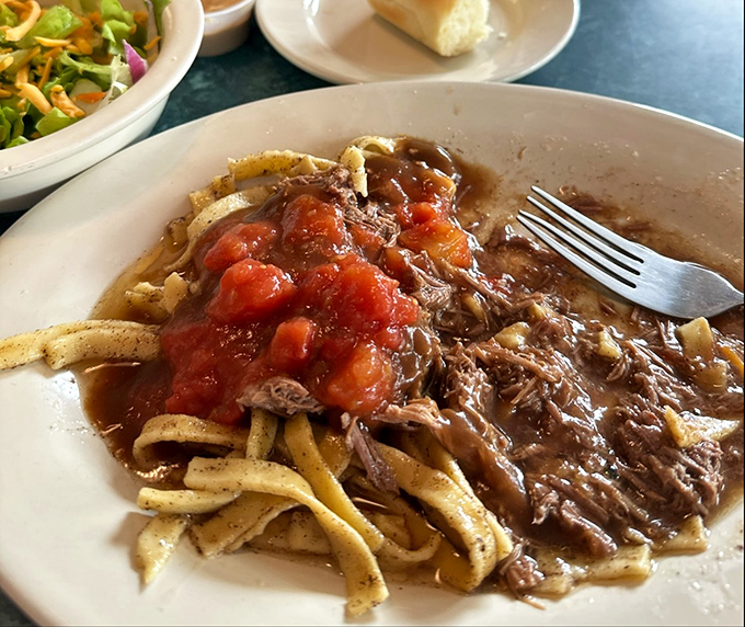 Pot roast over noodles with a side of stewed tomatoes—the kind of plate that makes you want to hug the chef and adopt their entire family.