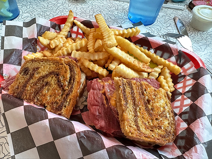 The Reuben sandwich in its natural habitat—perfectly grilled rye, meat stacked higher than your weekend plans, surrounded by a golden moat of crinkle-cut fries.