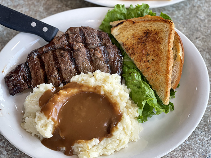 A perfectly grilled ribeye that doesn't need a fancy steakhouse setting to shine, accompanied by mashed potatoes drowning happily in gravy.