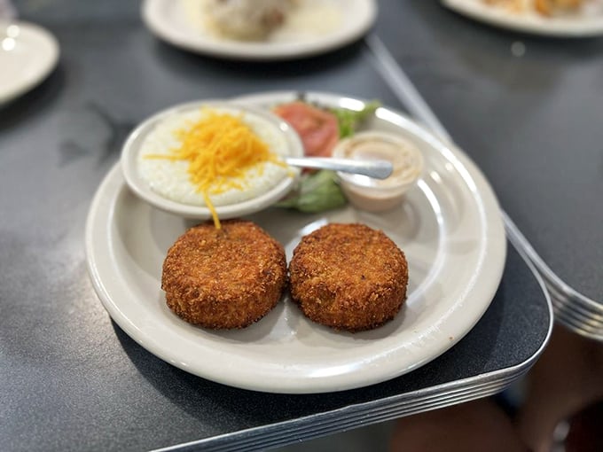 Golden-fried salmon croquettes stand at attention like delicious sentinels, guarding their treasure of creamy grits and fresh garnishes—a Southern breakfast tradition worth setting alarms for.