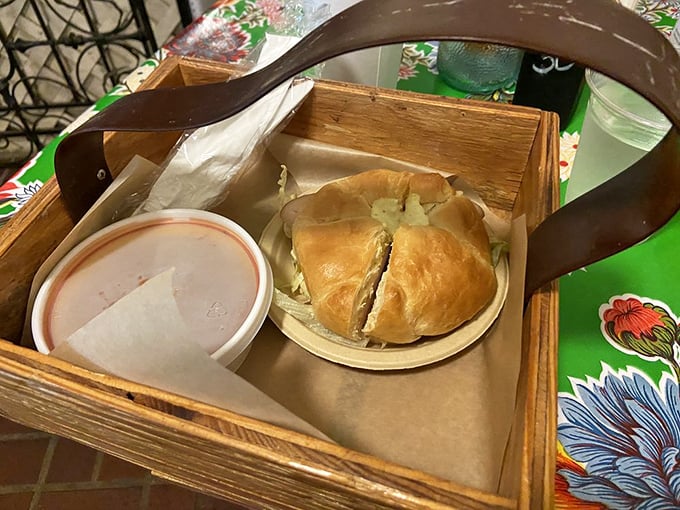 Not just any croissant—this golden vessel cradles what appears to be turkey, served in a rustic wooden carrier that somehow makes everything taste better.