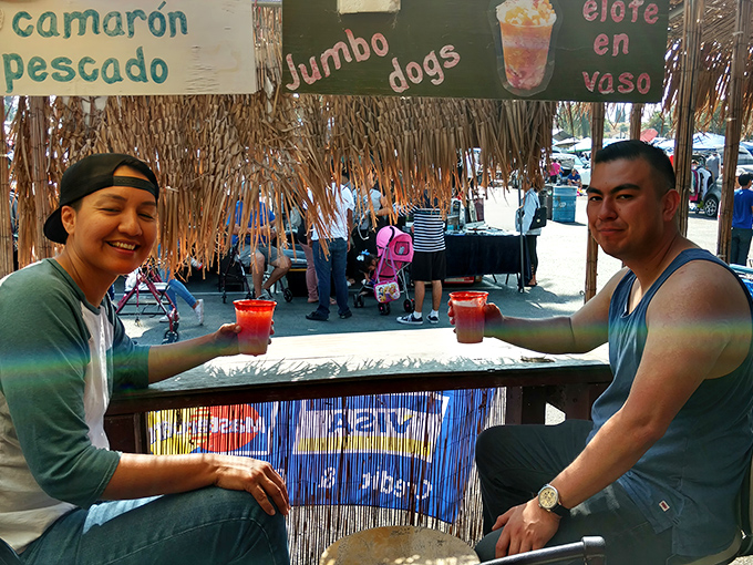 A thatched-roof refreshment stand offers the perfect pit stop—colorful drinks in hand, these shoppers have mastered the art of swap meet hydration.