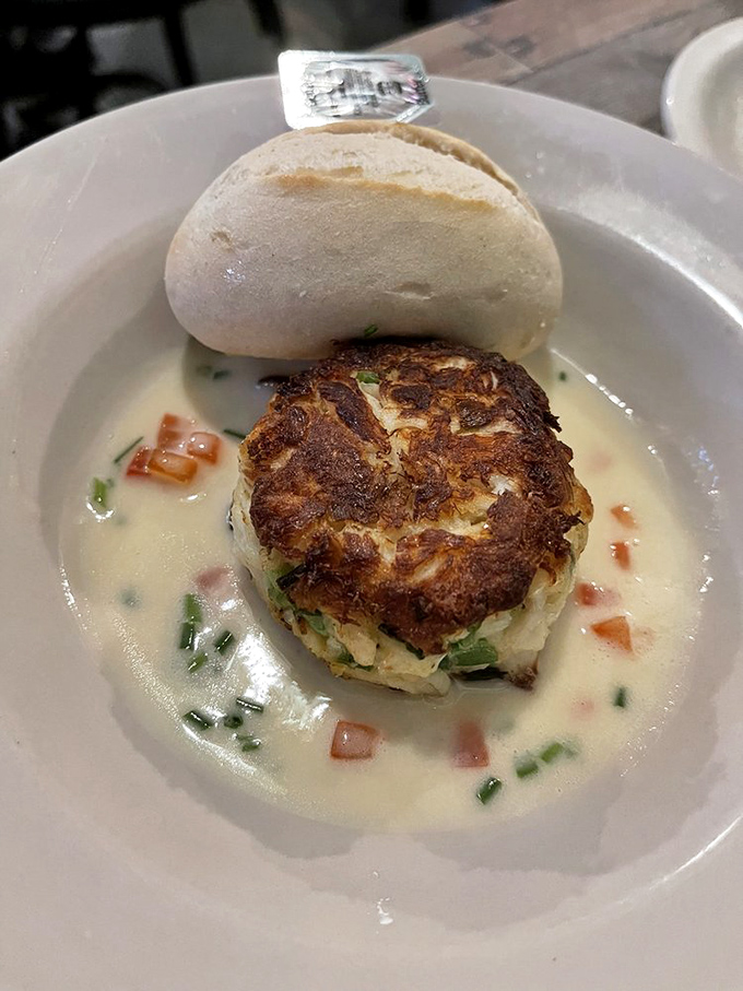 This crab cake isn't hiding behind fillers or fancy presentation—just pure crab flavor swimming in a delicate cream sauce with a roll standing by.